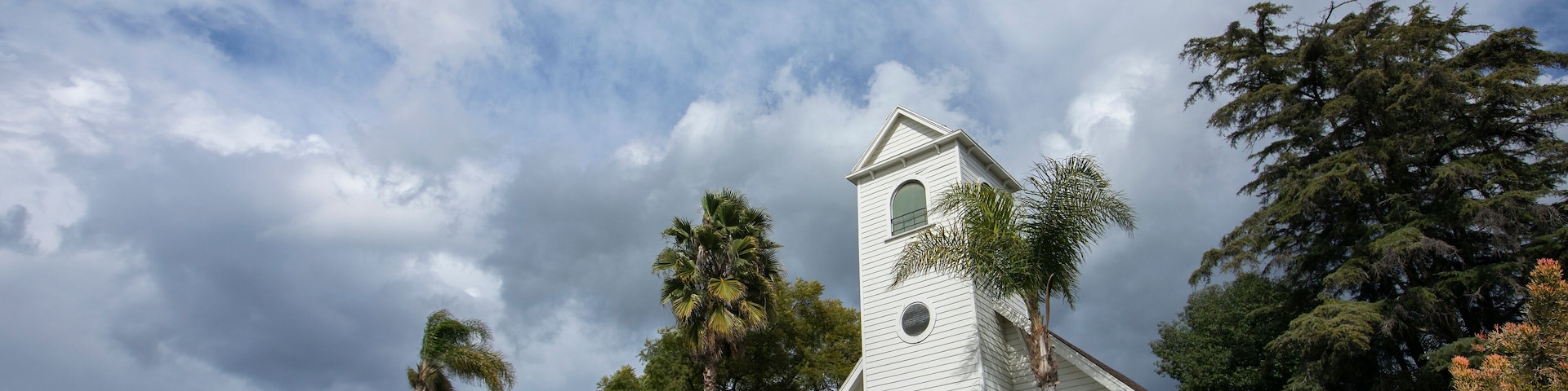 Uma igreja branca com um campanário, rodeada por vegetação exuberante e palmeiras.