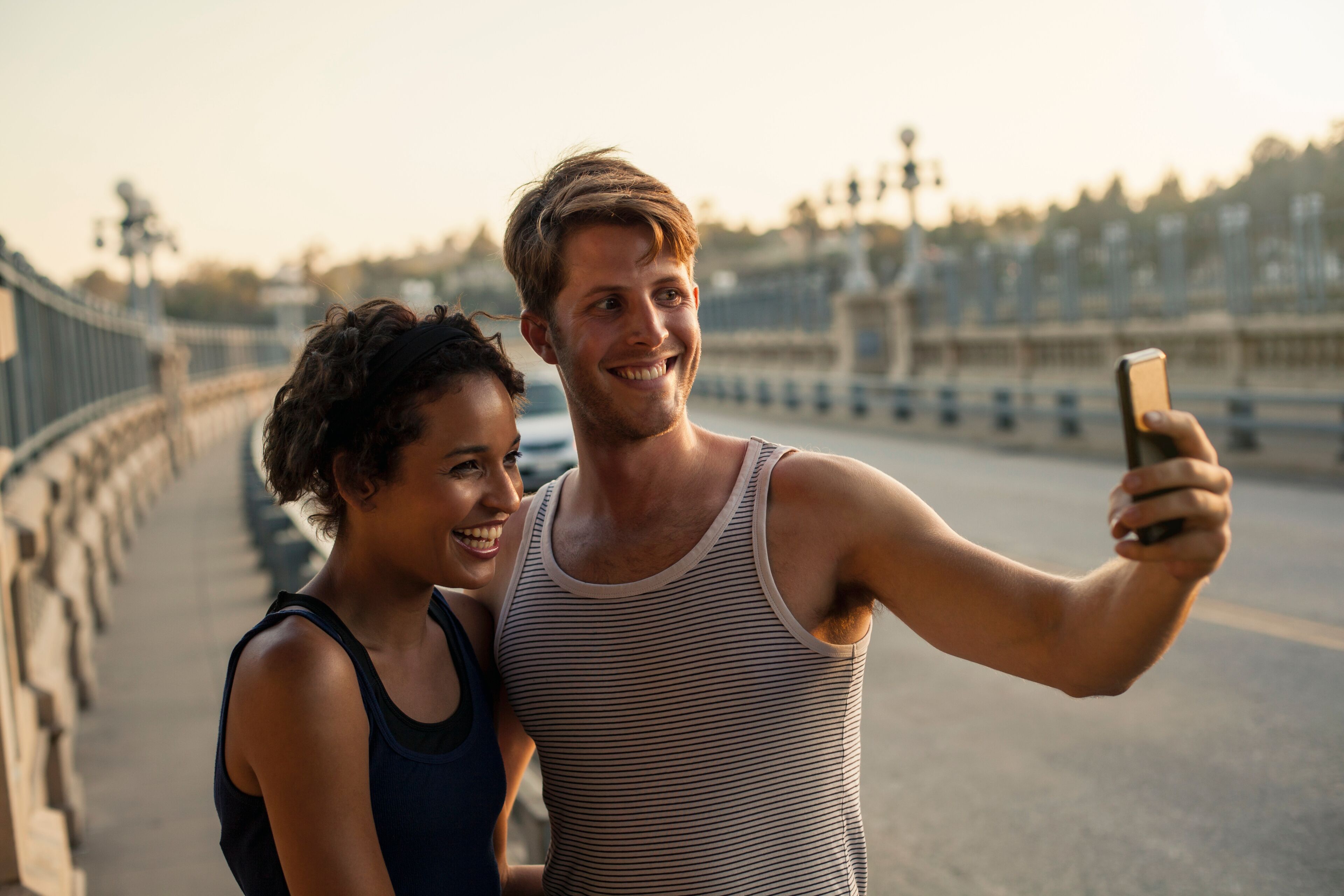 Uma pessoa tira um selfie em uma ponte, com paisagem urbana ao fundo.