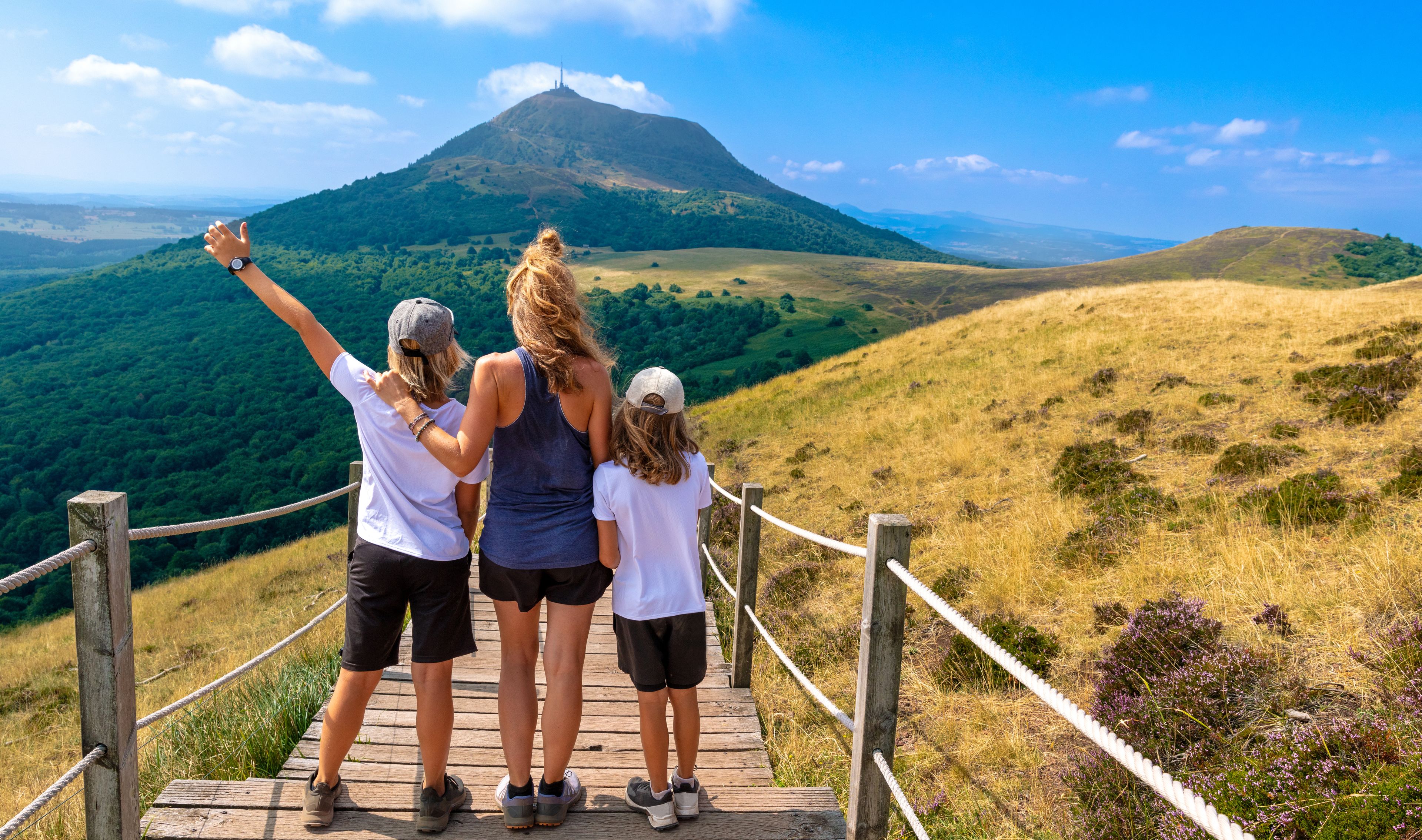 Uma família em um deck de madeira com vista para uma paisagem montanhosa sob um céu claro.