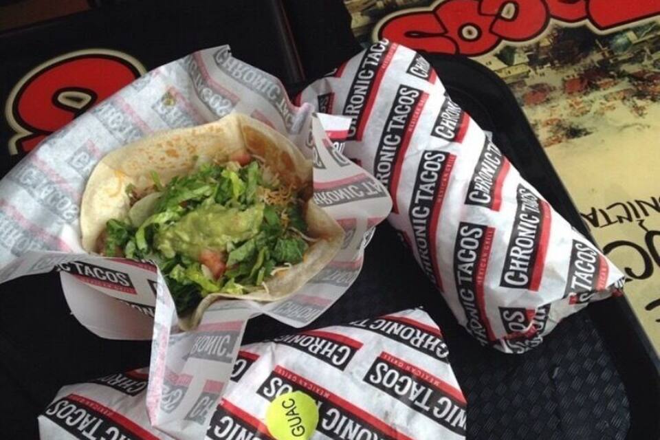 Taco embrulhado em bandeja preta com a marca 'Chronicle Tacos'.