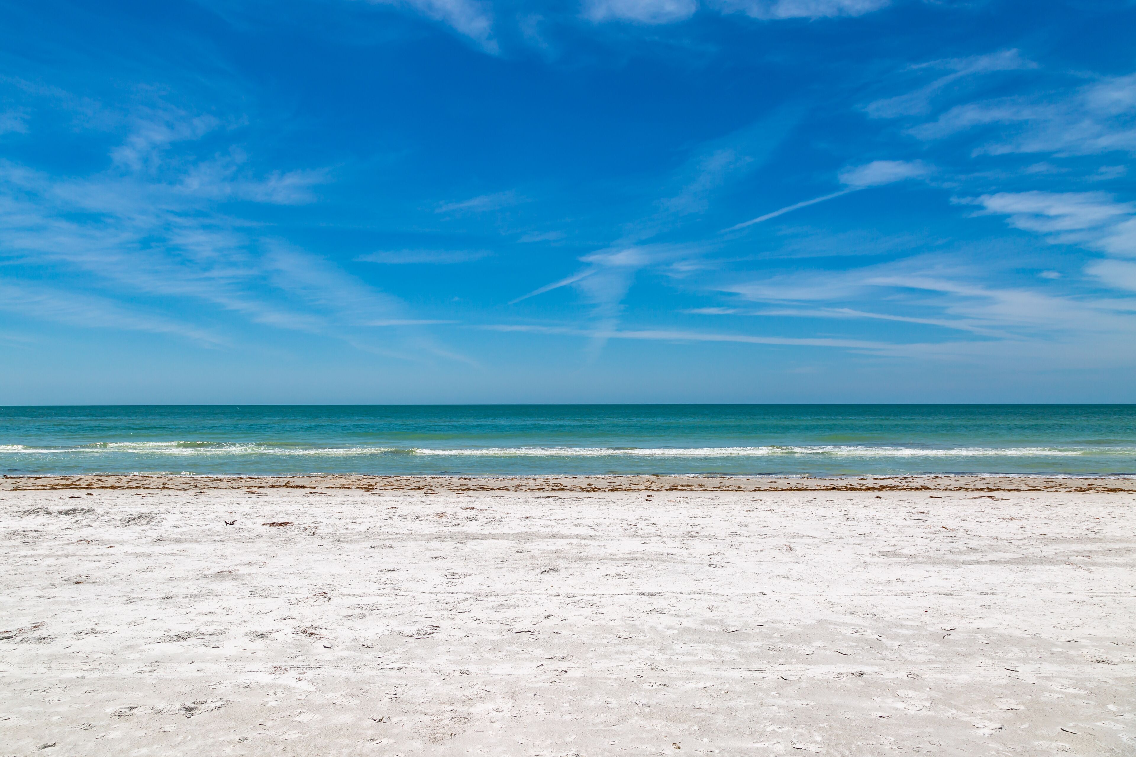 Uma praia com areia branca e céu azul e límpido.