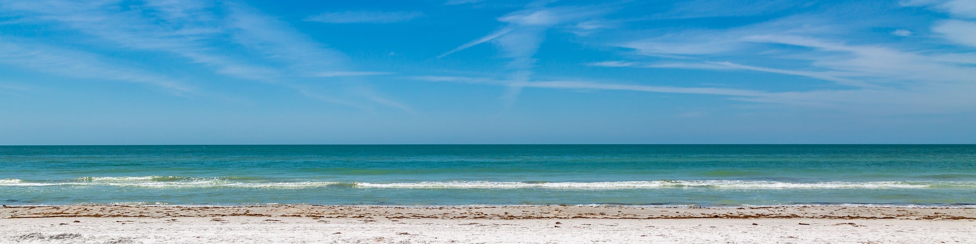Uma praia com areia branca e céu azul e límpido.