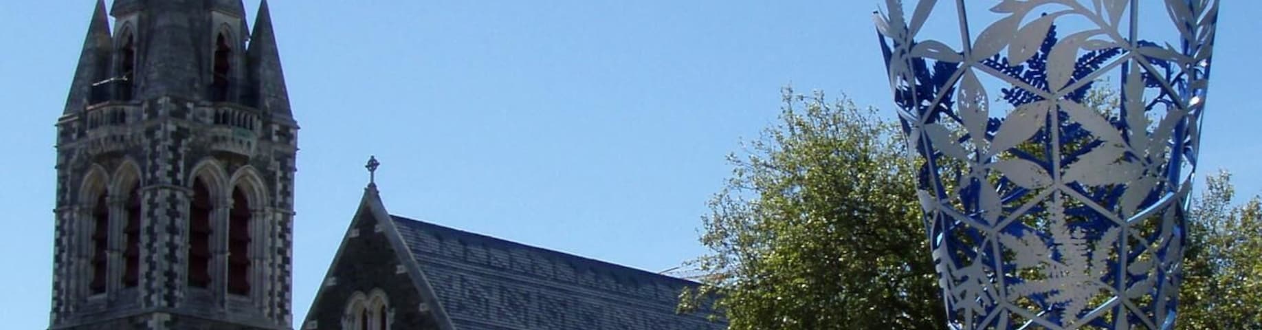 Uma igreja histórica com uma torre alta e uma grande escultura decorativa de metal numa praça pública.