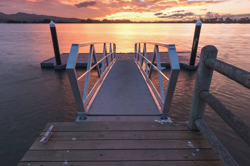 Um píer de madeira que se estende sobre águas calmas sob um céu ao pôr do sol.