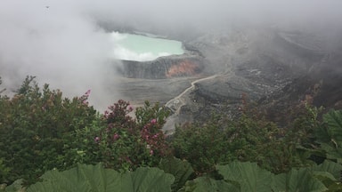 Paisagem vulcânica com um lago azul-turquesa, rodeada por terreno acidentado e vegetação densa.