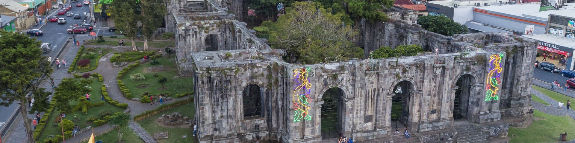 Estrutura de pedra antiga com decorações coloridas, cercada por um jardim bem cuidado e uma rua movimentada.