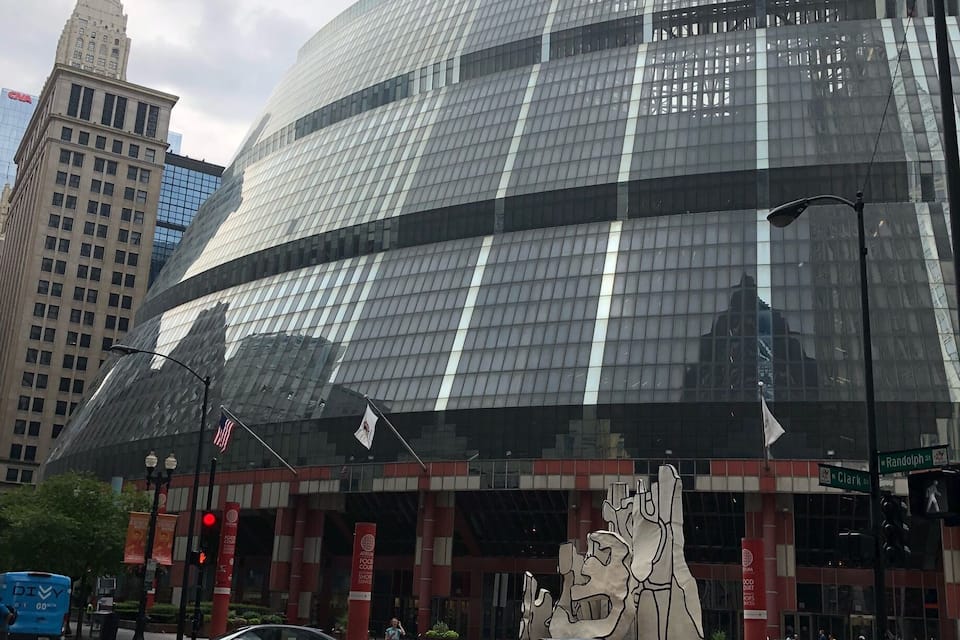 Um edifício moderno de vidro com fachada curva, rodeado por ruas urbanas e outros edifícios altos.