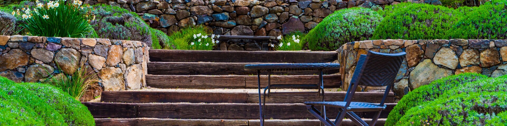 Um jardim com um muro de pedra, degraus de madeira e mobiliário de exterior.