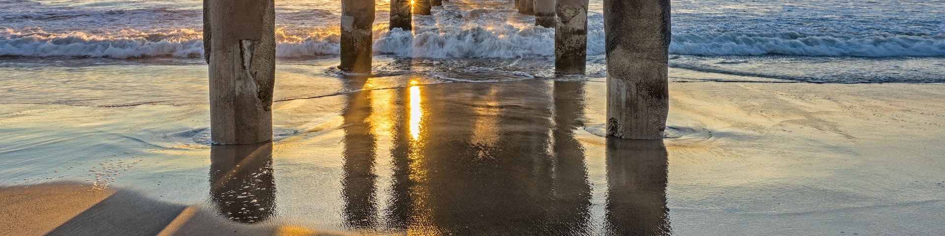 Um cais se estende para o oceano enquanto ondas quebram ao pôr do sol.
