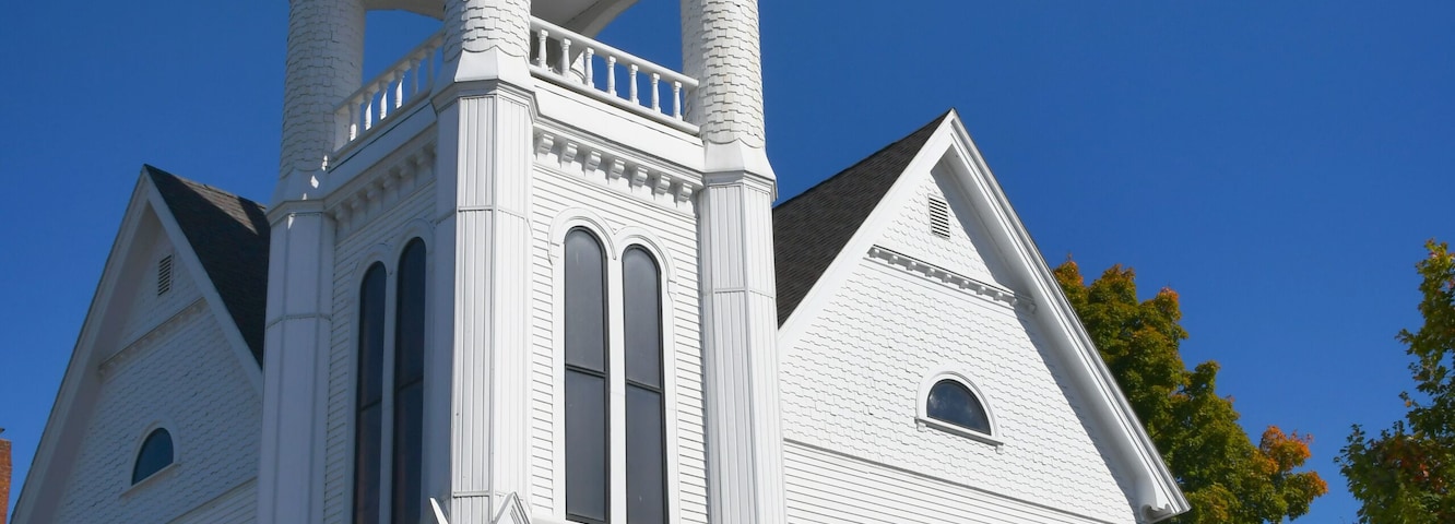 Uma igreja branca com porta vermelha, uma torre de sino e um pináculo.