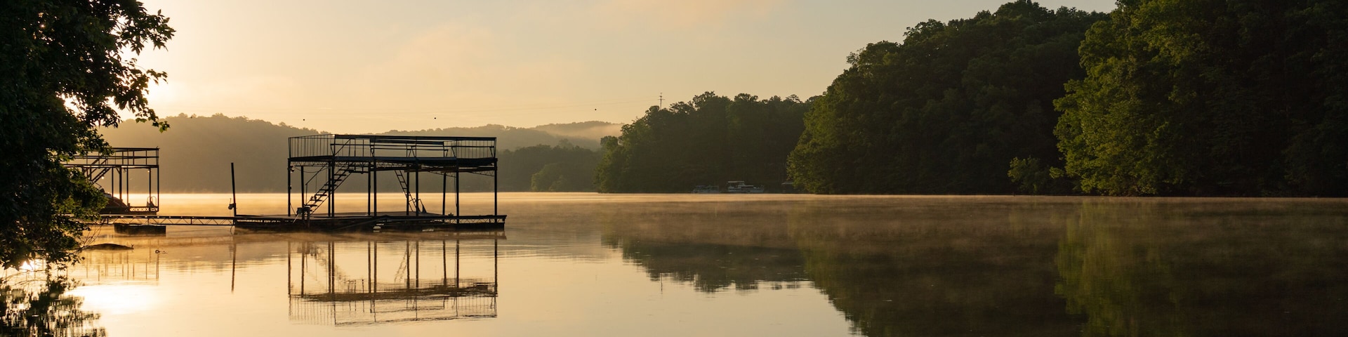 Um lago calmo com um cais e uma colina arborizada ao fundo.