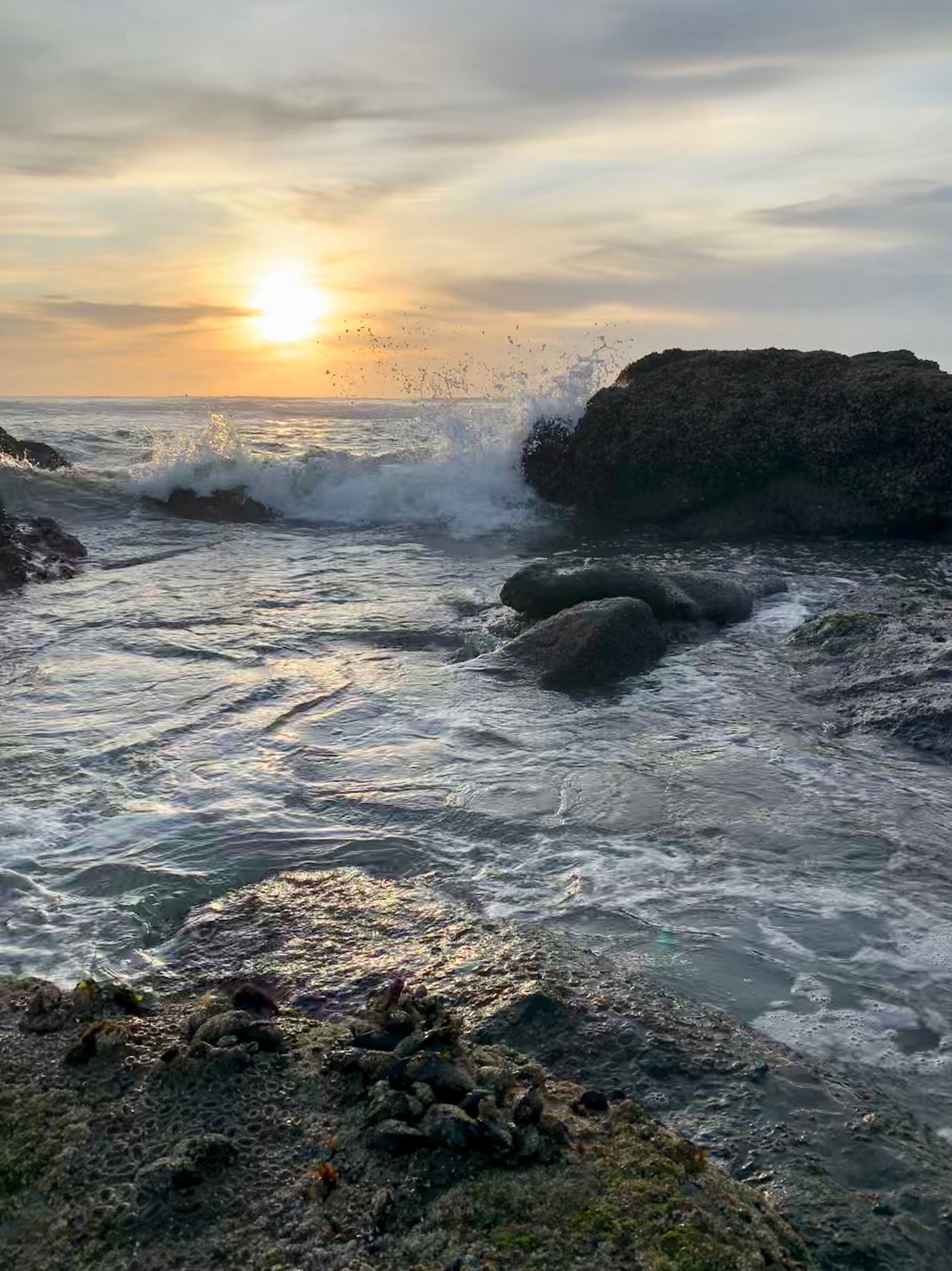 Uma costa rochosa com ondas quebrando nas pedras ao pôr do sol.