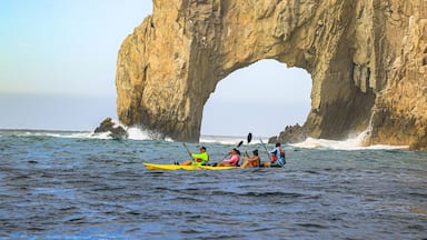 Um grupo pratica caiaque sob uma formação rochosa natural em arco.
