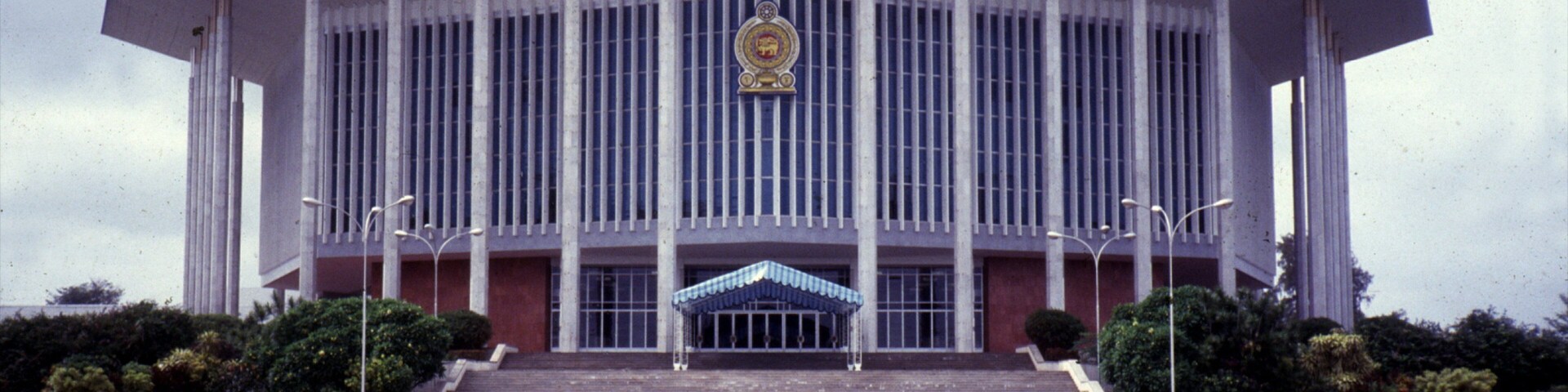Um edifício grande e moderno, com entrada central e uma fonte em frente.