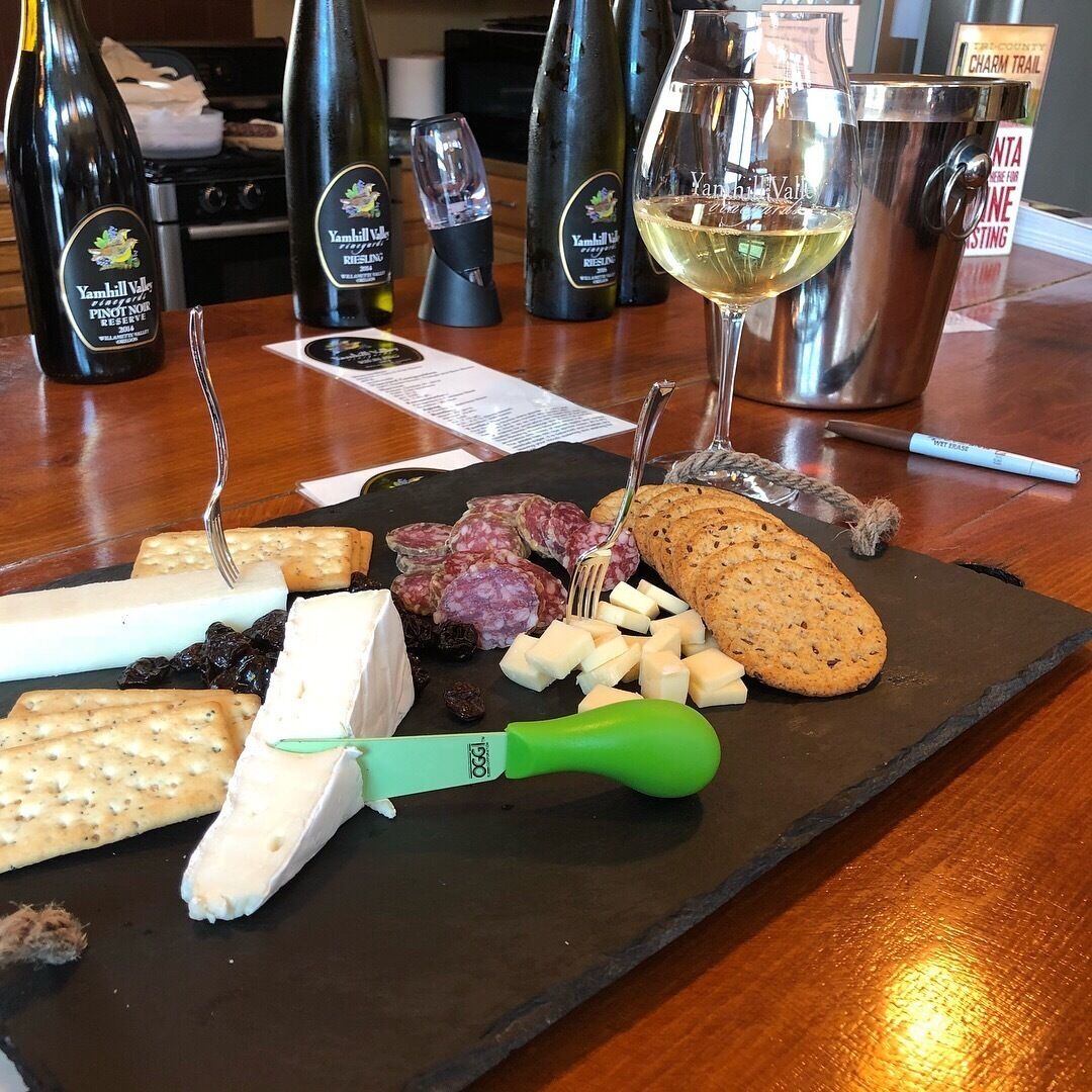 Tábua de frios com queijos, carnes, biscoitos e uma garrafa de vinho sobre uma base de ardósia.