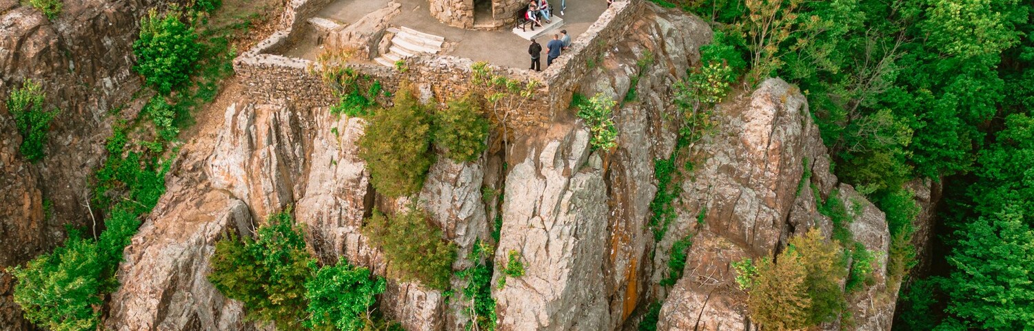 Uma torre de pedra rodeada por floresta densa e terreno rochoso.