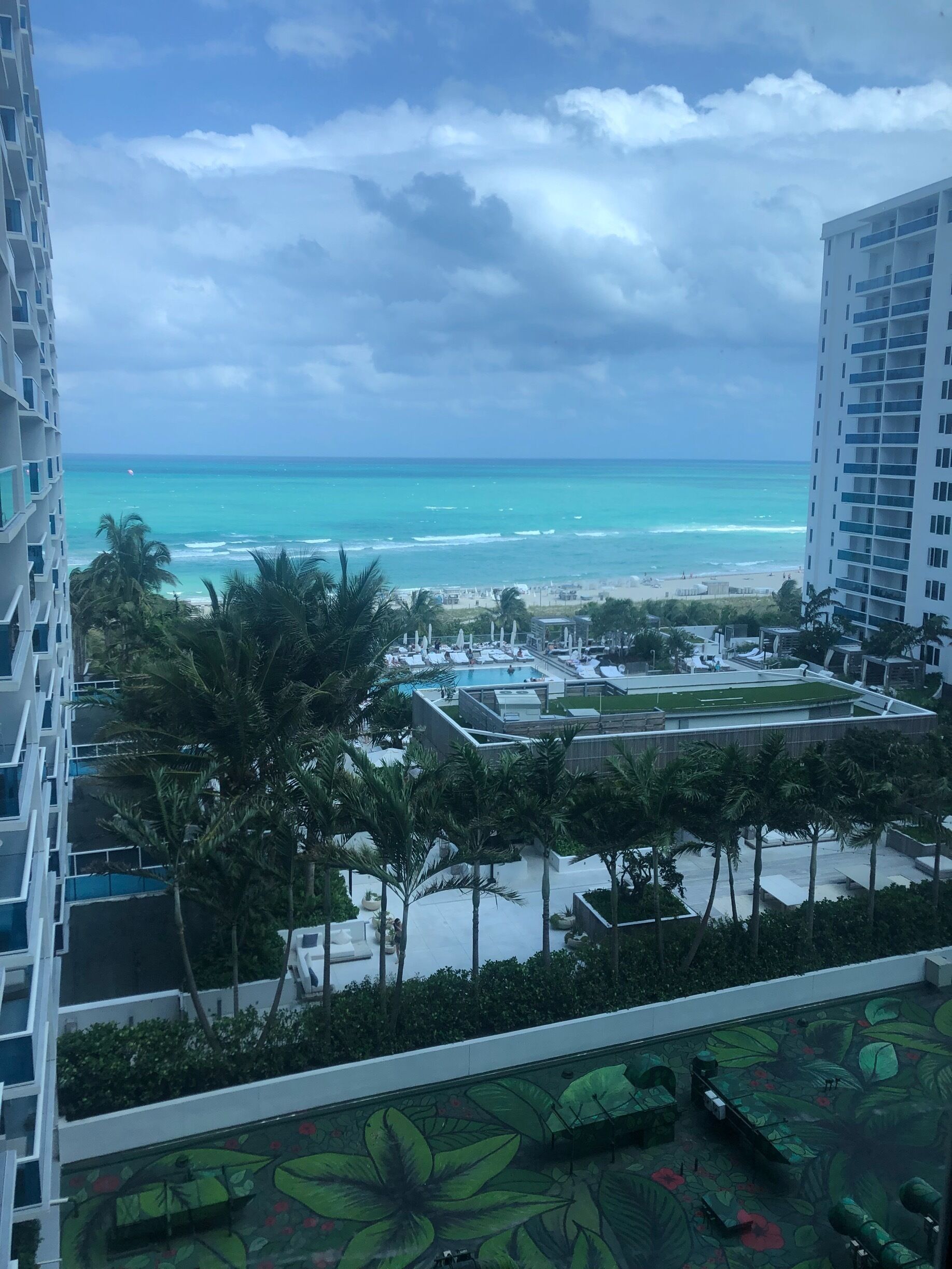 Um resort com piscina, palmeiras e uma praia ao fundo.