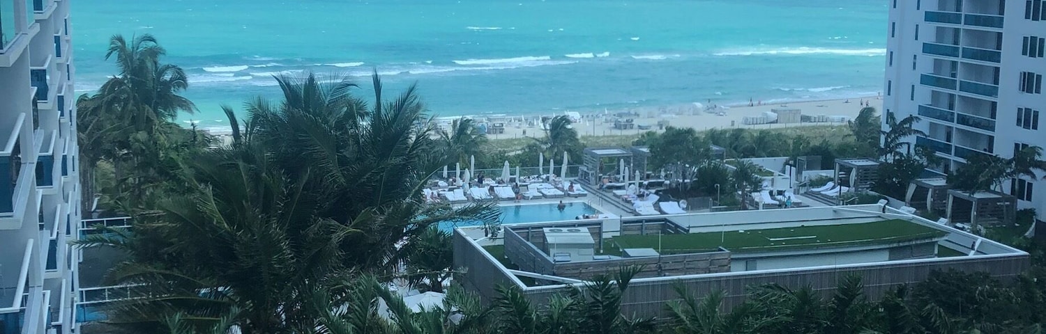 Um resort com piscina, palmeiras e uma praia ao fundo.