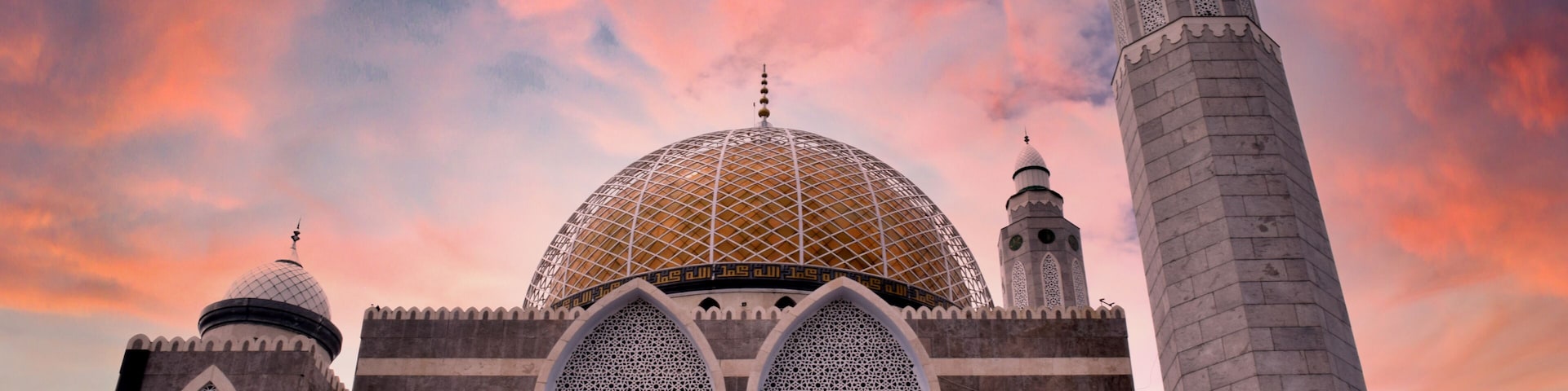 Uma mesquita com uma cúpula grande e minaretes contra o céu do pôr do sol.