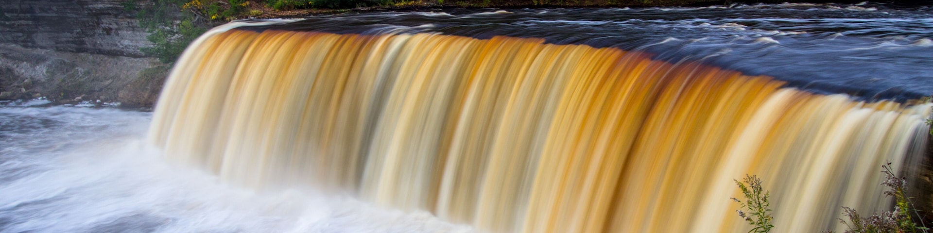 Uma cascata desce sobre um afloramento rochoso, cercada por folhagem de outono.