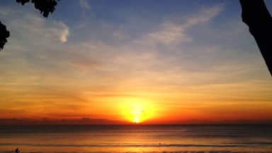 Um pôr do sol sobre o oceano com a silhueta de uma pessoa na praia.