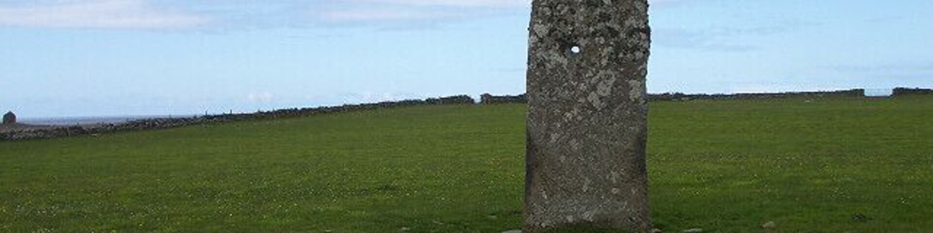 Um monumento de pedra vertical num campo relvado sob um céu nublado.