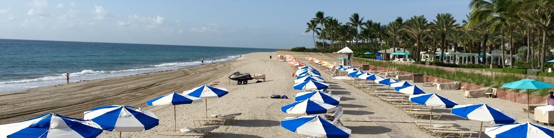 Uma praia com fileiras de guarda-sóis e espreguiçadeiras azuis e brancas.