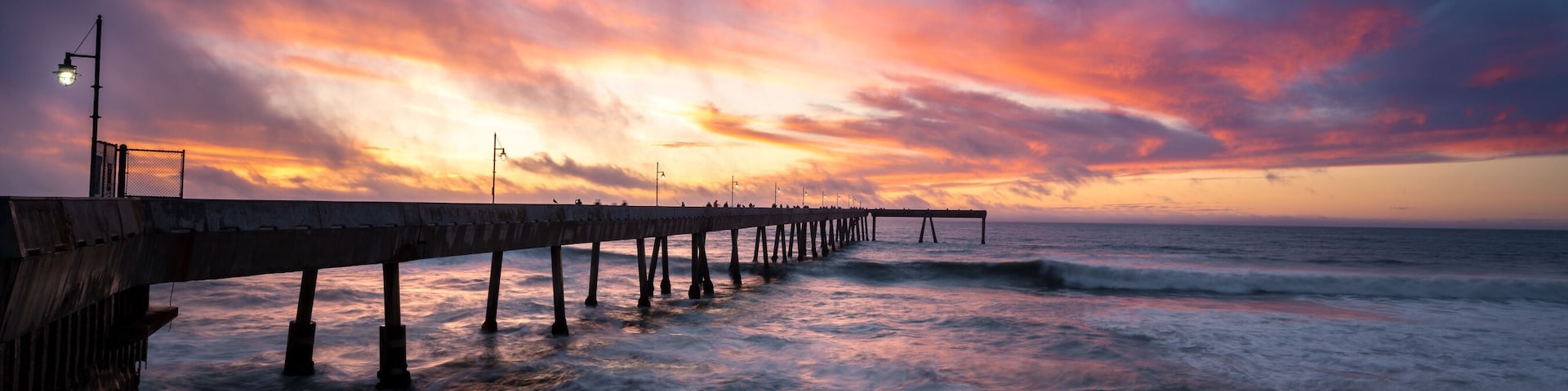 Um píer que se estende para o oceano, com o pôr do sol ao fundo.