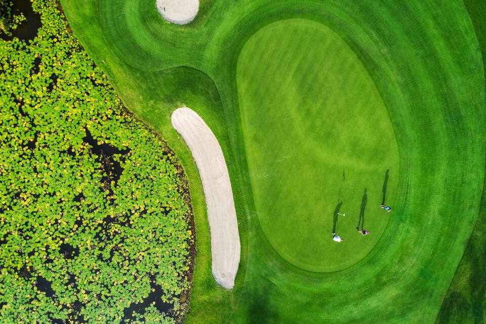 Vista aérea de um campo de golfe com um bunker de areia, obstáculos de água e um putting green.