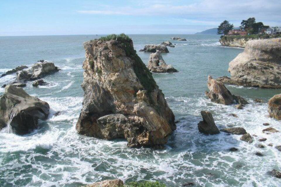 Litoral rochoso com ondas quebrando contra grandes pedras e falésias.