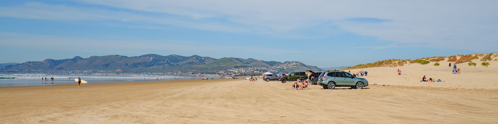 Uma praia de areia com veículos e pessoas.