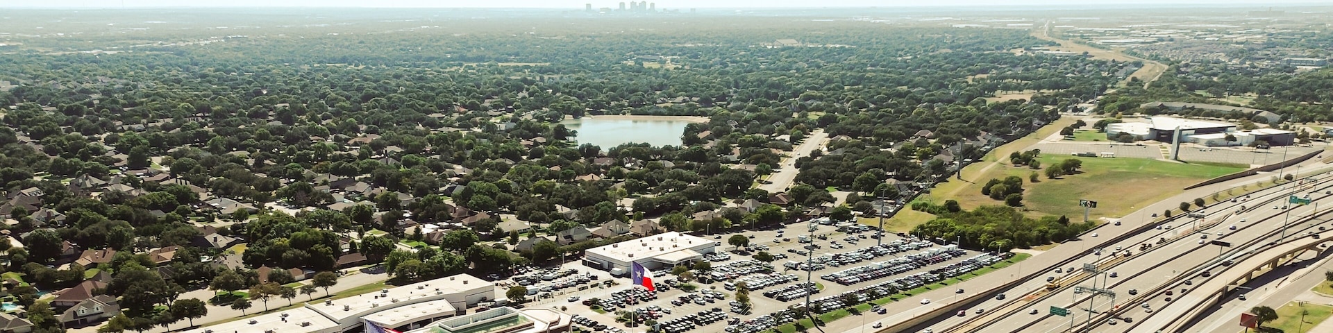 Vista aérea de uma área suburbana com um amplo estacionamento, um edifício com a bandeira americana e uma rodovia.