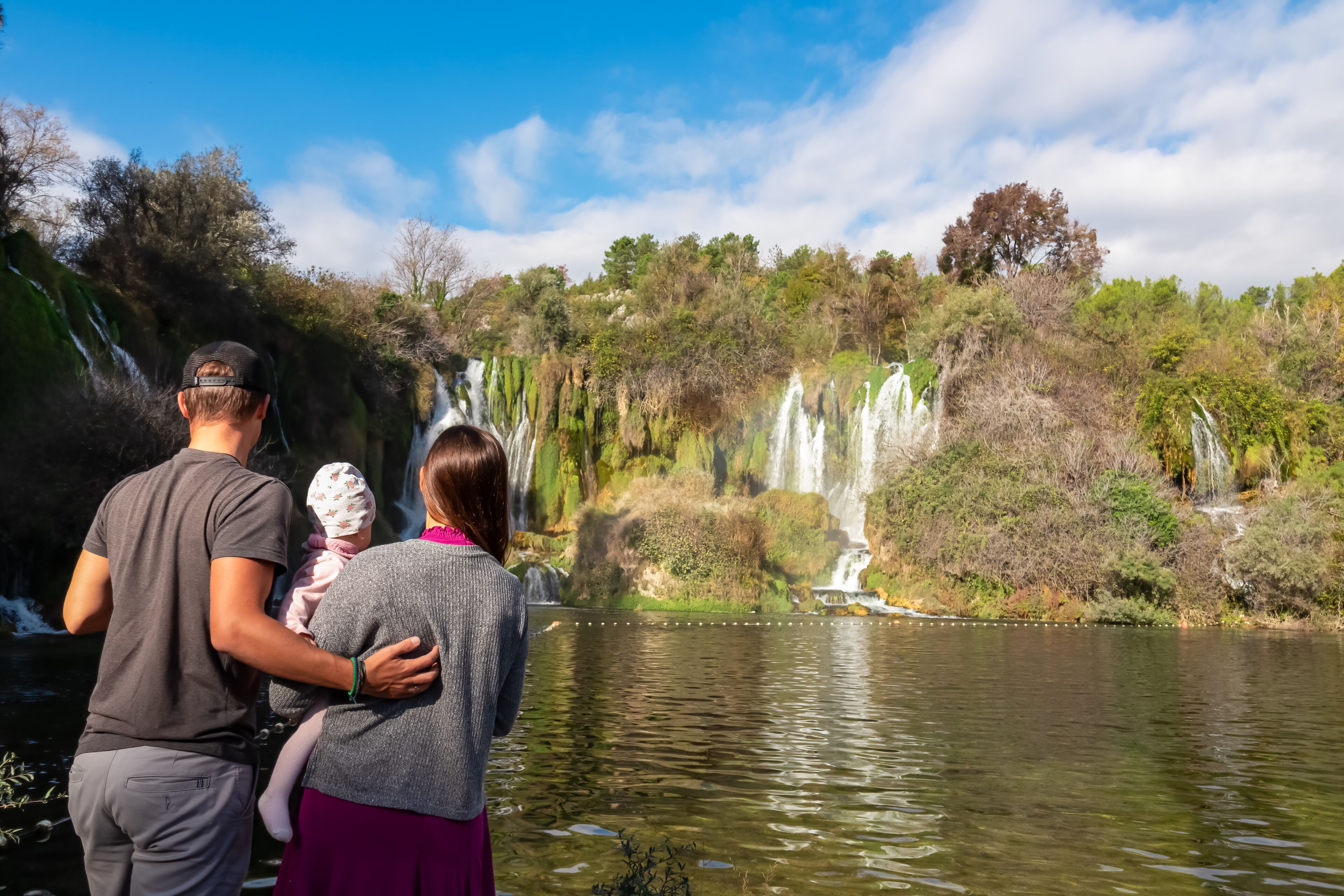Uma família parada perto de um rio com várias cachoeiras e vegetação exuberante.