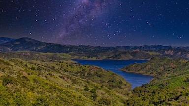 Céu estrelado sobre uma paisagem montanhosa com um lago.