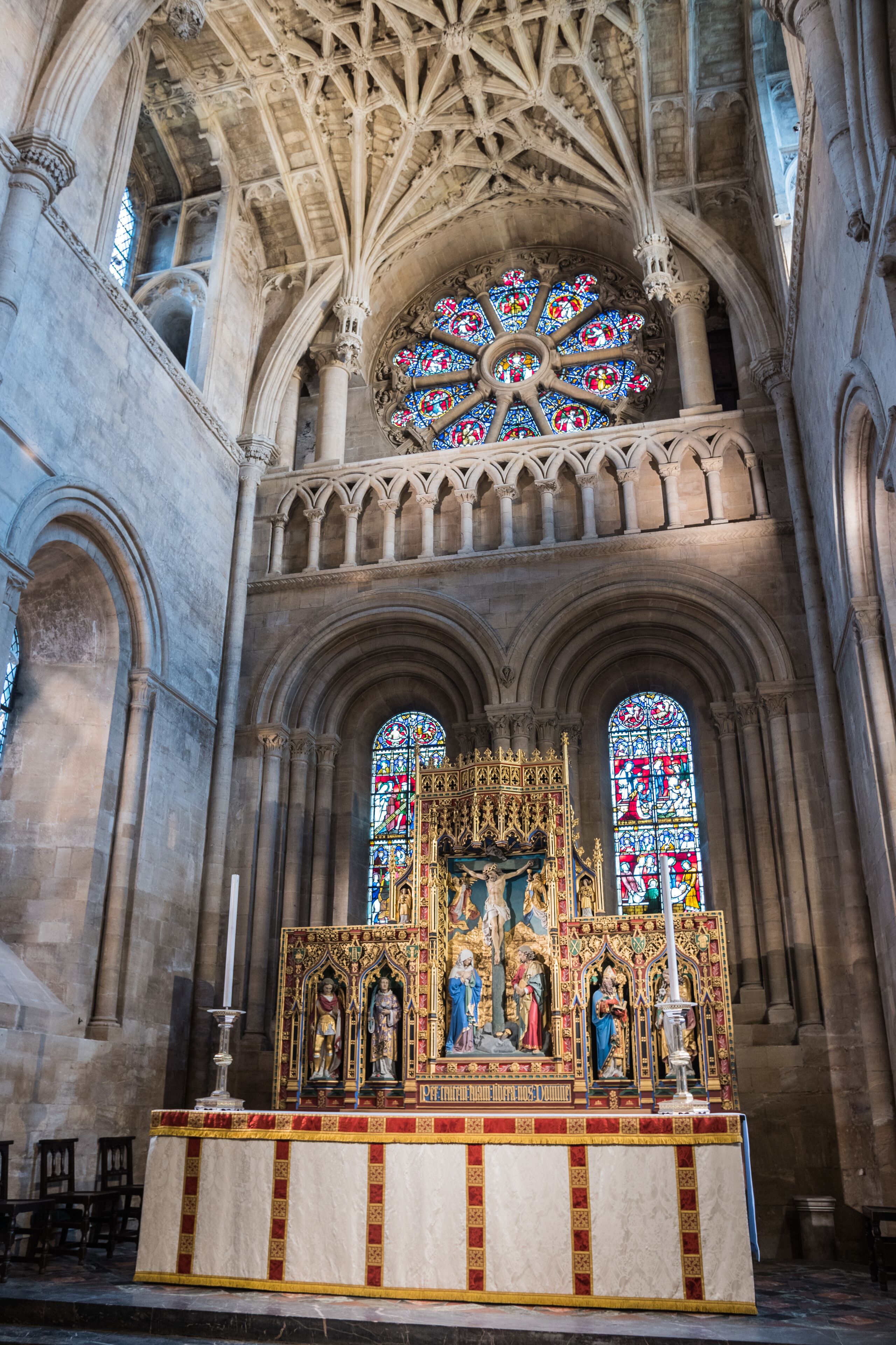 Interior de uma catedral com arquitetura gótica, vitrais coloridos e um altar ricamente decorado.