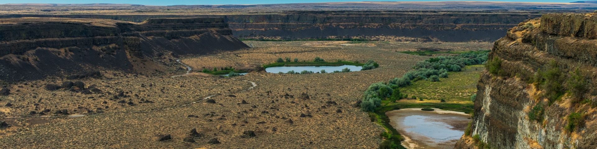 Um vasto cânion com um rio serpenteando por ele, rodeado por vegetação escassa e terreno rochoso.