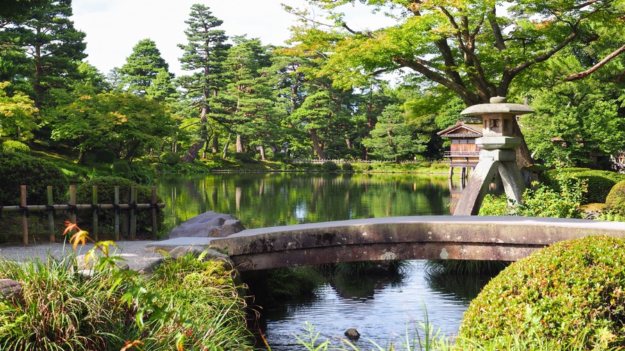 Um jardim japonês tranquilo, com lago, lanterna de pedra e estruturas de madeira tradicionais.