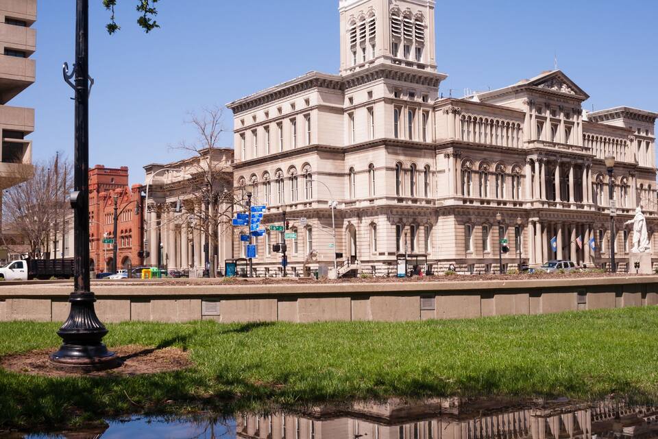 Um edifício histórico com uma torre do relógio, um poste de luz e um reflexo em uma poça.
