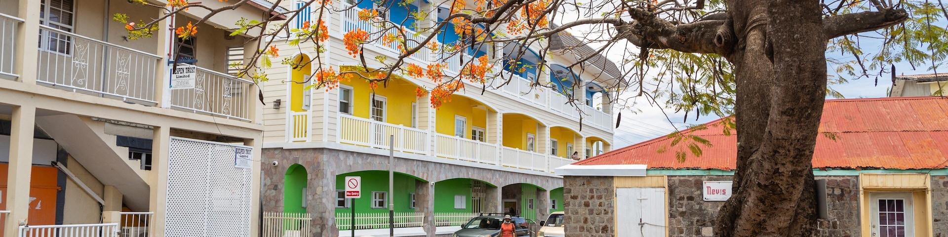 Um edifício colorido com varandas, uma árvore em primeiro plano e um sinal de 'Proibido o Acesso'.