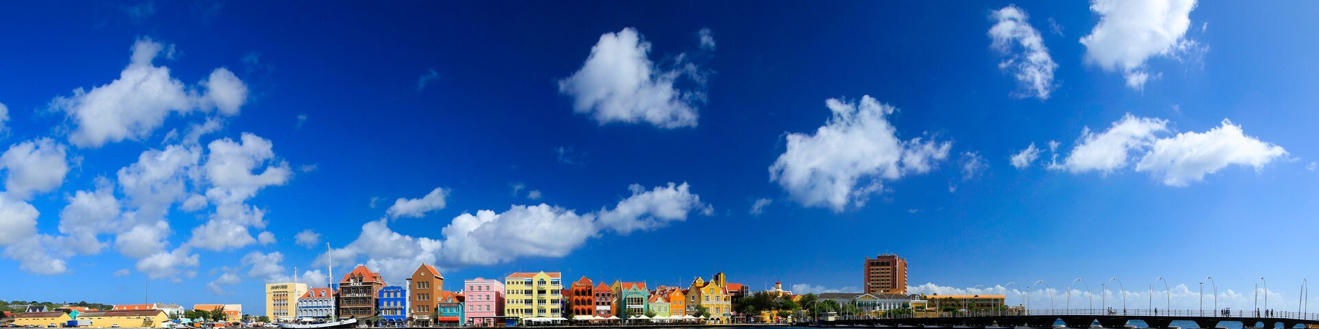 Paisagem urbana à beira-mar, com edifícios coloridos, uma ponte e um céu azul límpido.