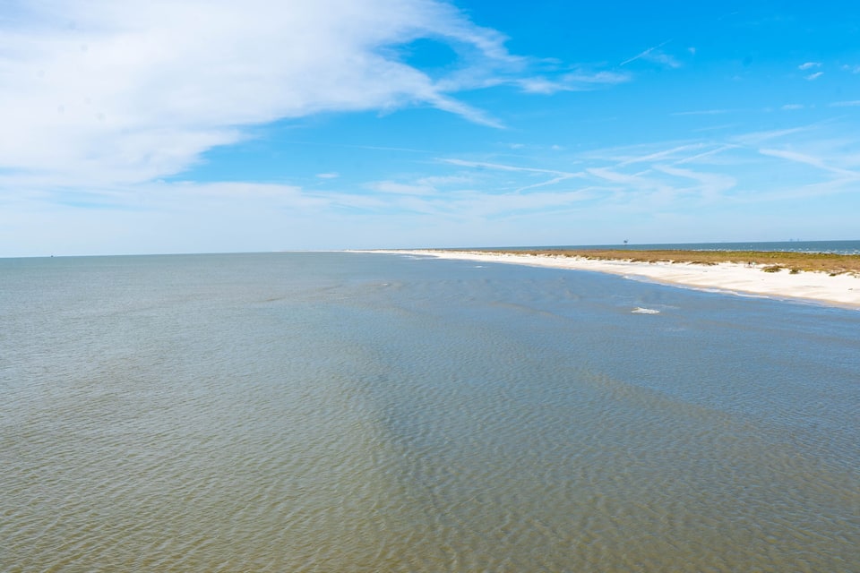 Uma praia extensa com águas cristalinas, areal arenoso e um navio ao longe.