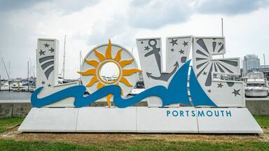 Um letreiro à beira-mar com um sol, ondas e estrelas, e a palavra 'PORTSMOUTH' na parte inferior.