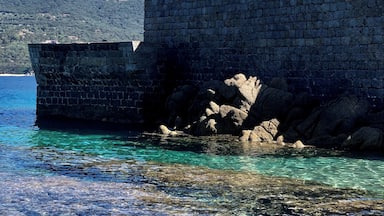 Um farol com a parte superior verde, uma parede de pedra e água azul cristalina.