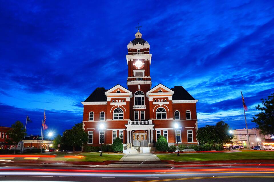 Um grande edifício da justiça em tijolo com torre de relógio, cercado por um gramado bem cuidado e postes de iluminação.