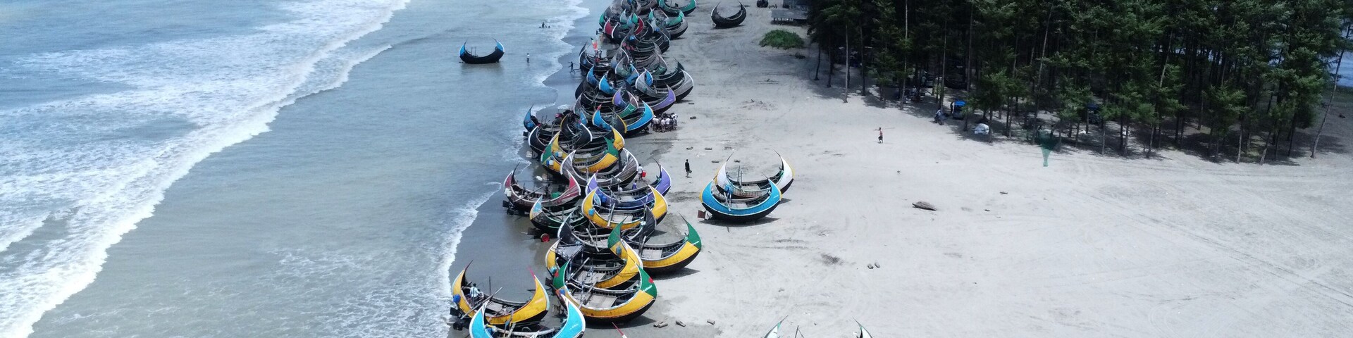 Uma praia com vários barcos tradicionais enfileirados na margem, areal arenoso e uma floresta densa ao fundo.