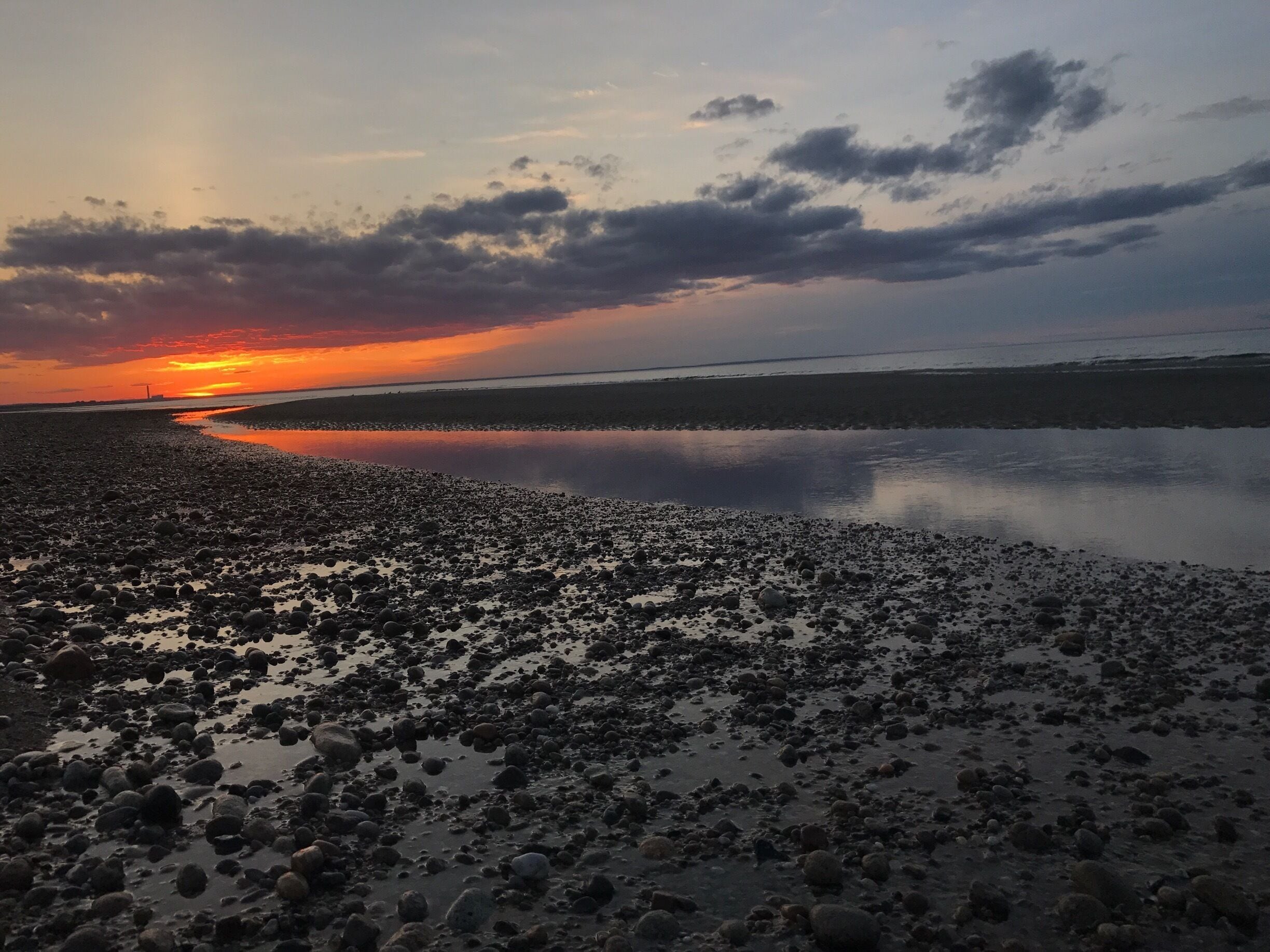 Uma praia rochosa ao pôr do sol, com o mar calmo refletindo o céu.