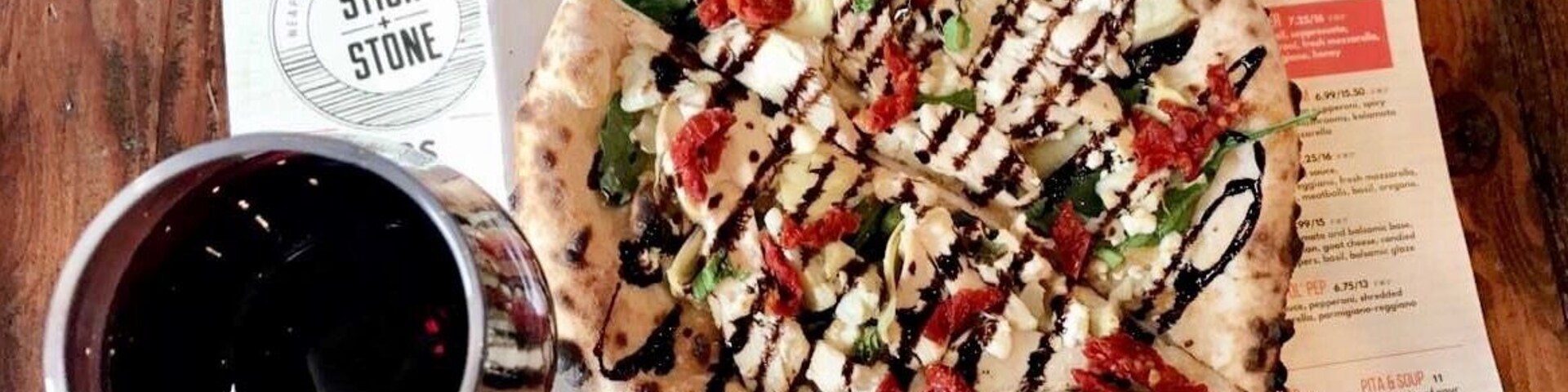 Uma pizza com ingredientes e um cardápio sobre uma mesa de madeira.