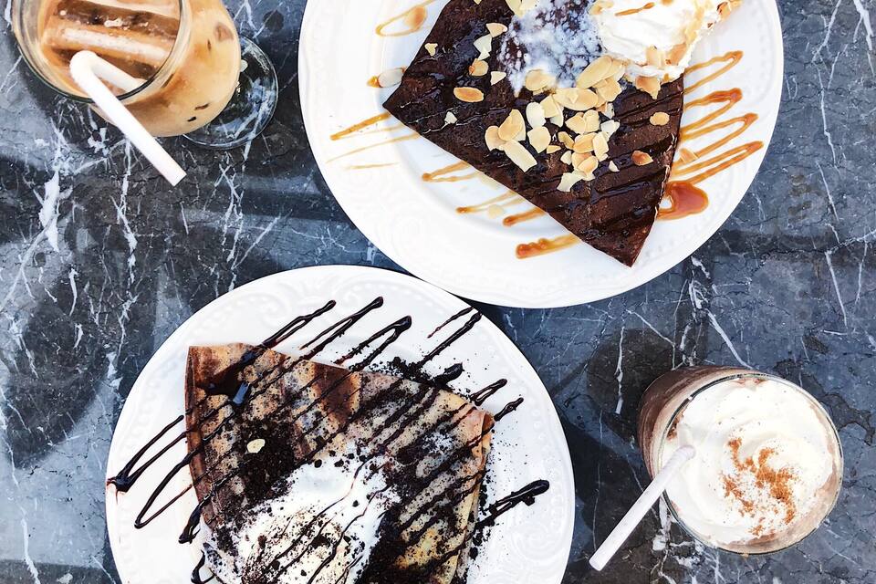 Um prato de sobremesa com brownie, chantilly e amêndoas, e um copo de café gelado.
