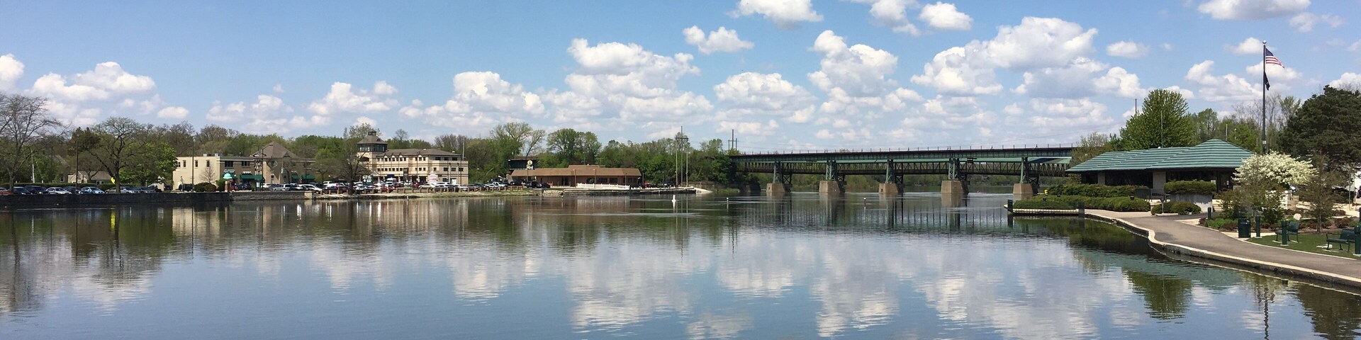 Um lago calmo com uma ponte ao fundo, rodeado por edifícios e árvores.