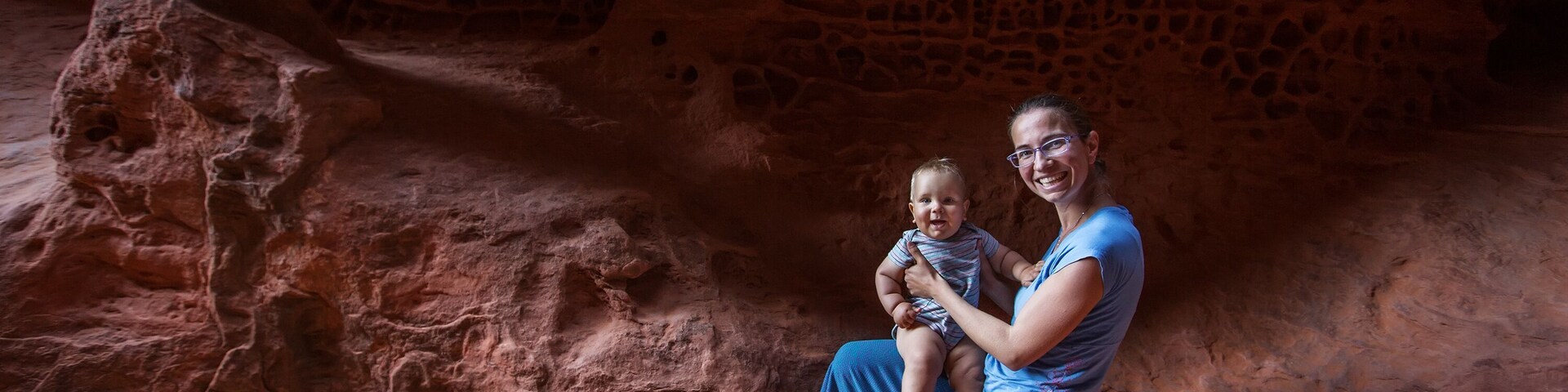 Uma pessoa segurando uma criança em uma caverna rochosa com paredes vermelhas.